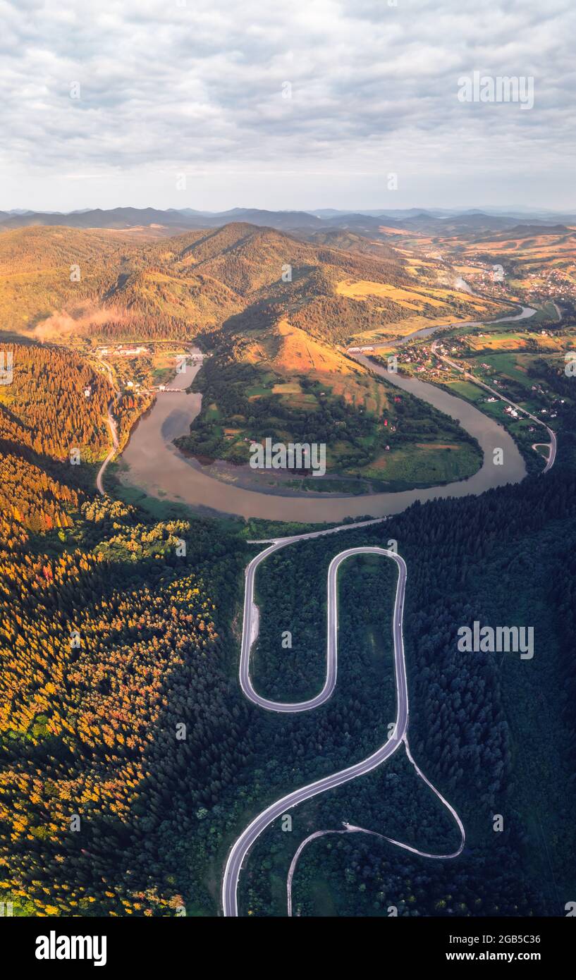 Aerial drone view over the autumn mountains with mountain road serpentine, river and forest ...