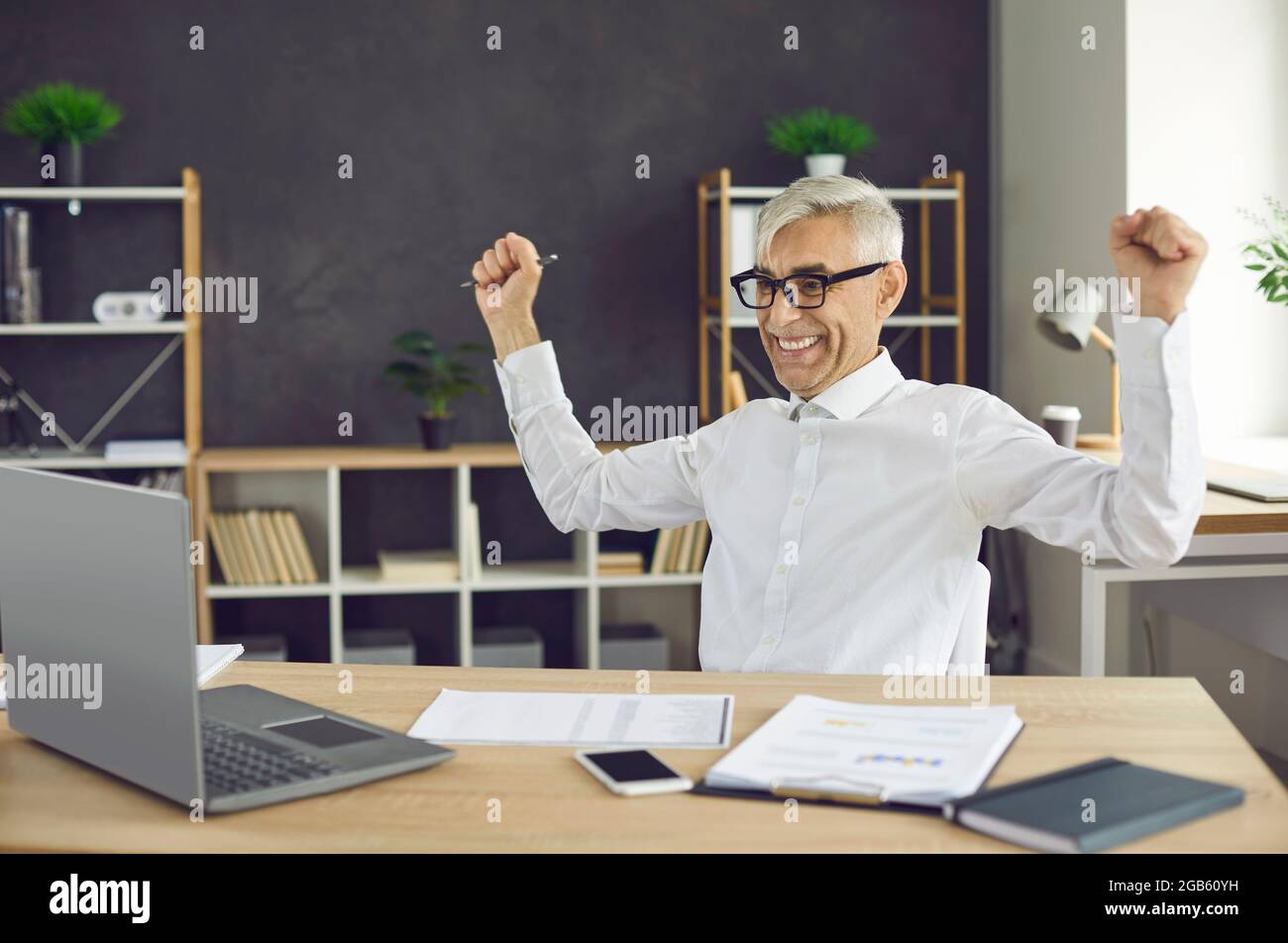Happy man sitting at office desk, looking at screen of laptop computer ...