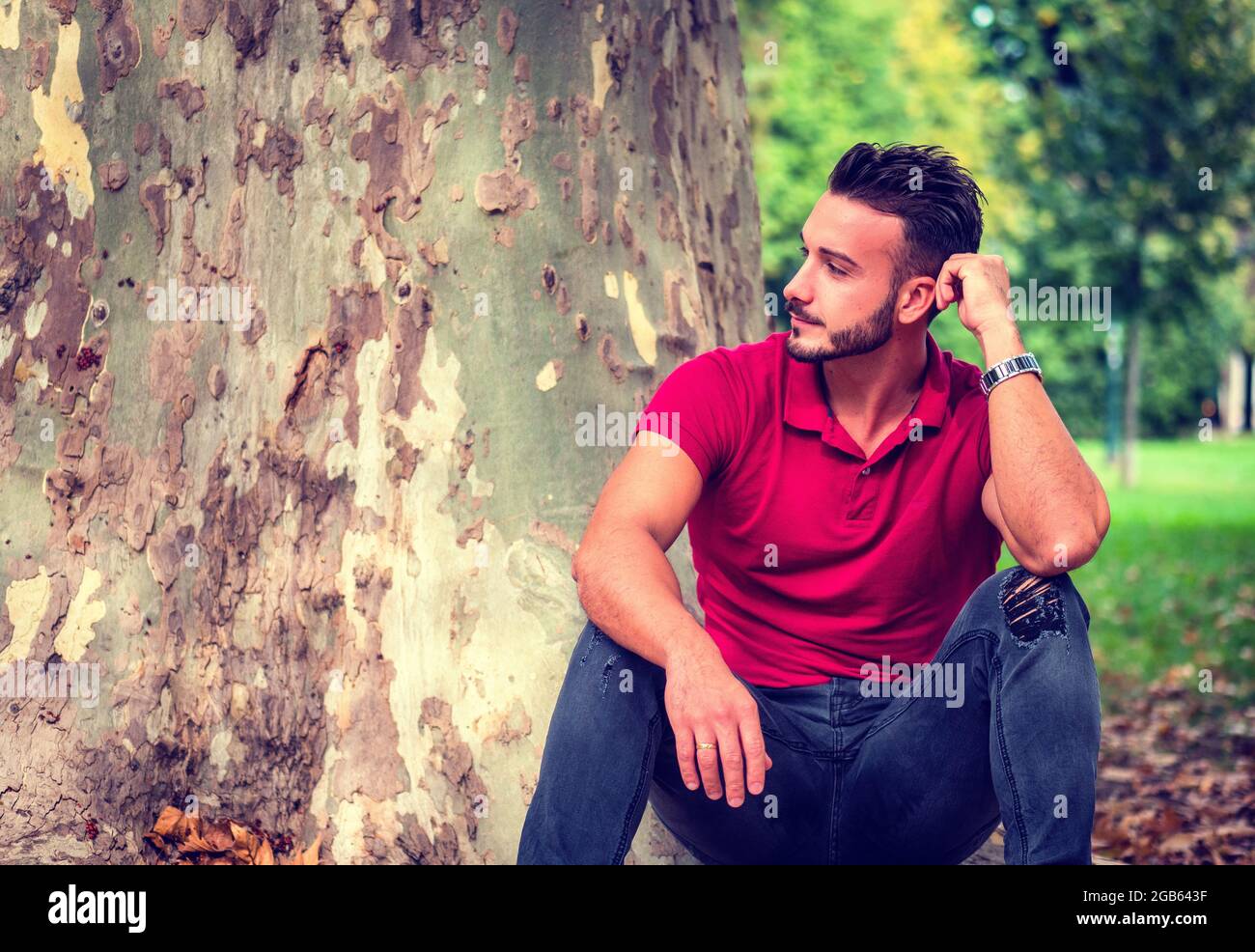 Attractive young man in park resting against tree Stock Photo - Alamy
