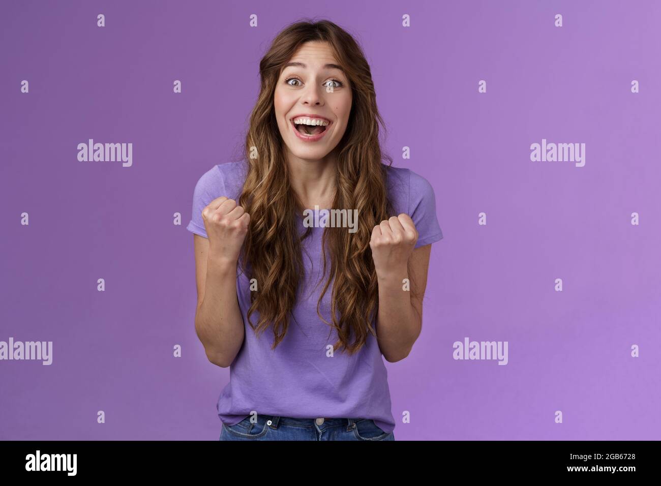 Cheerful cute devoted curly girl smiling broadly rooting for friend ...