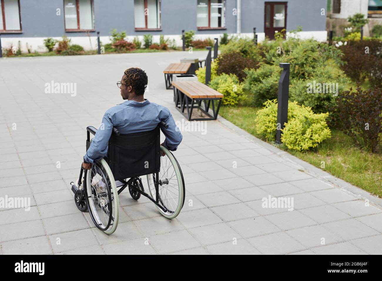 Rear view of African-American disabled man moving forward in wheelchair ...