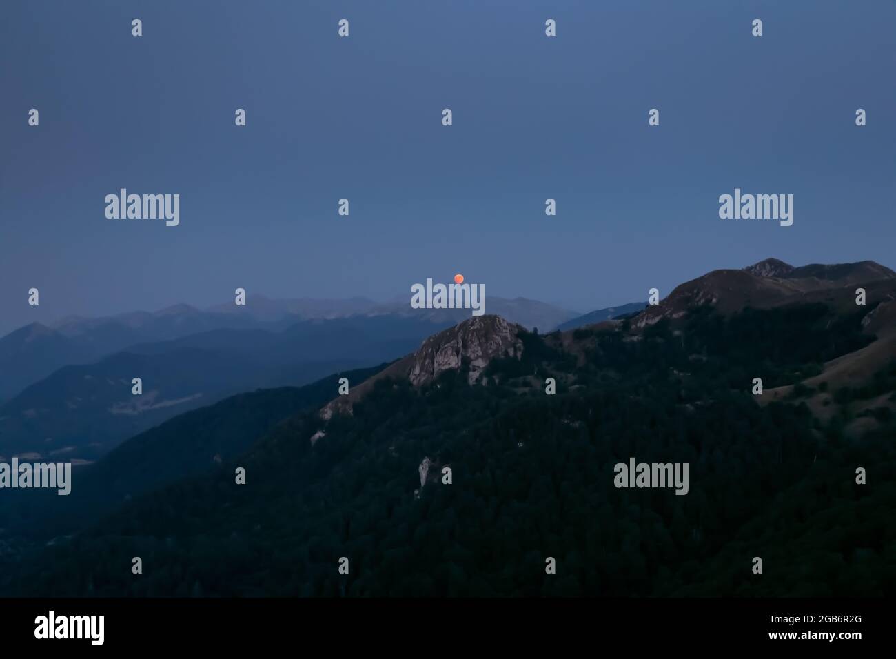 Splendid full red moon rises over the mountain ridges of the Apennines ...
