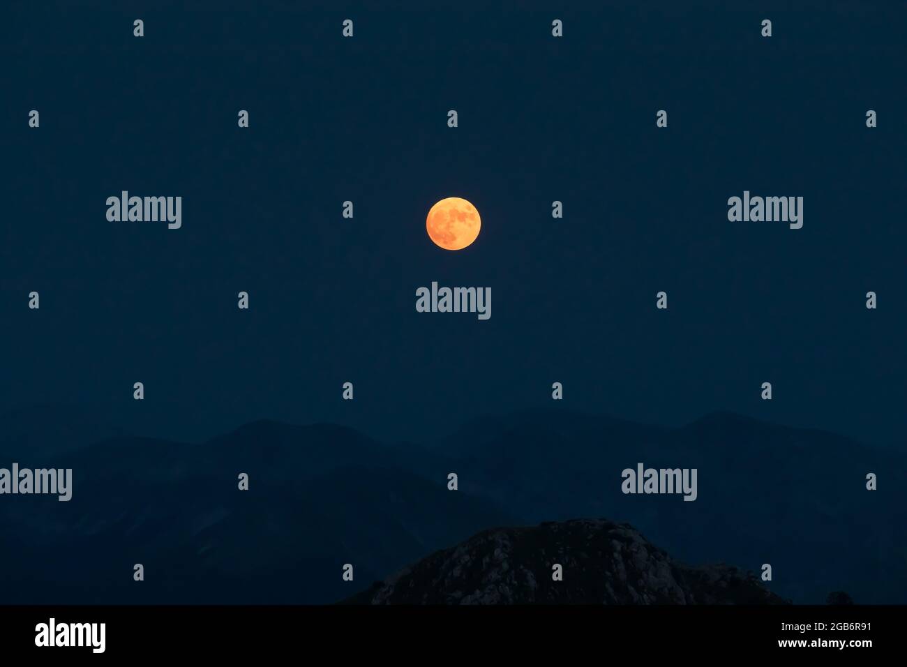 Splendid full red moon rises over the mountain ridges of the Apennines ...