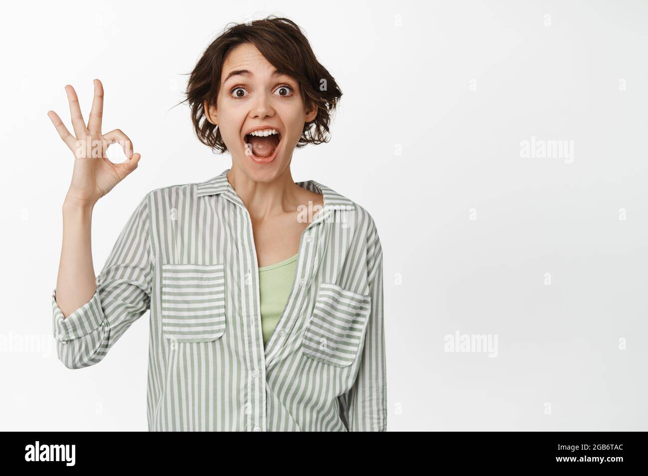 Surprised brunette girl shows okay, ok sign, look amazed, praise smth ...