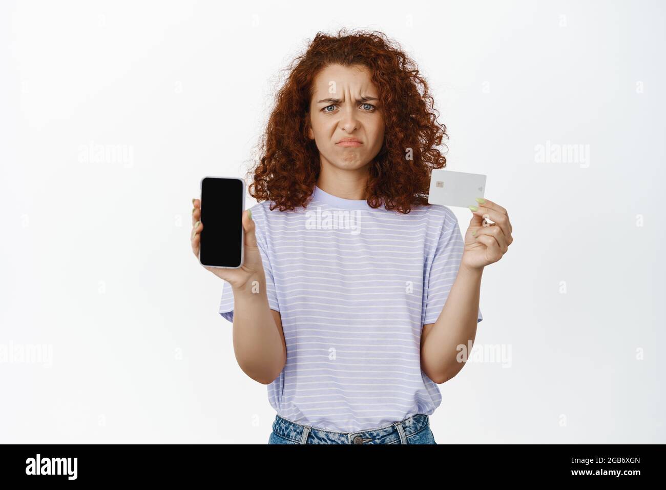 Disappointed redhead woman showing mobile phone screen, credit card ...