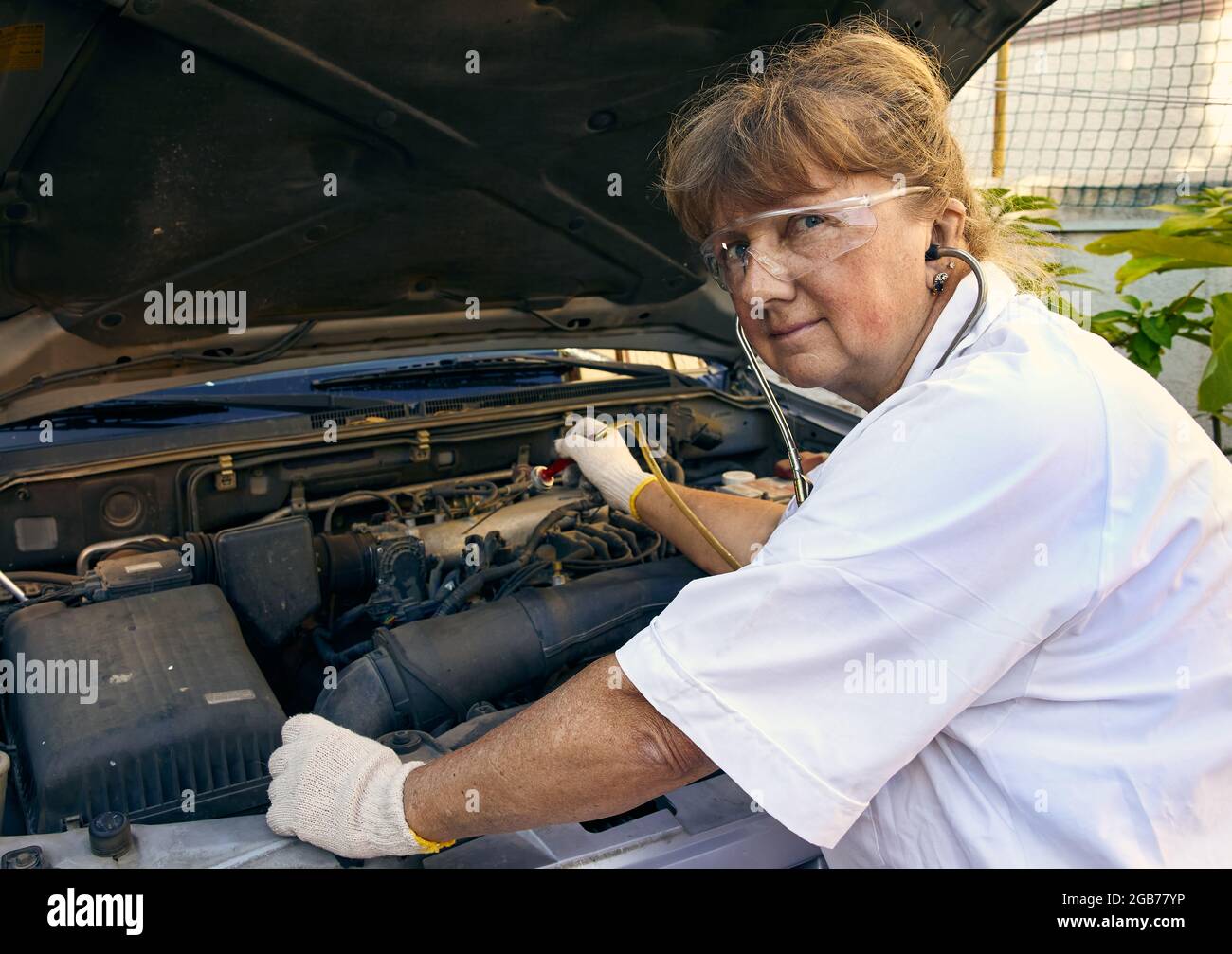 Car mechanic examining engine operation with a stethoscope. Woman with ...