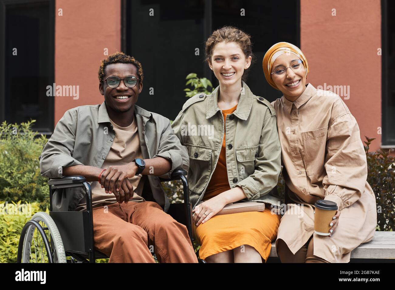 Group of positive young multi-ethnic friends sitting on bench and ...