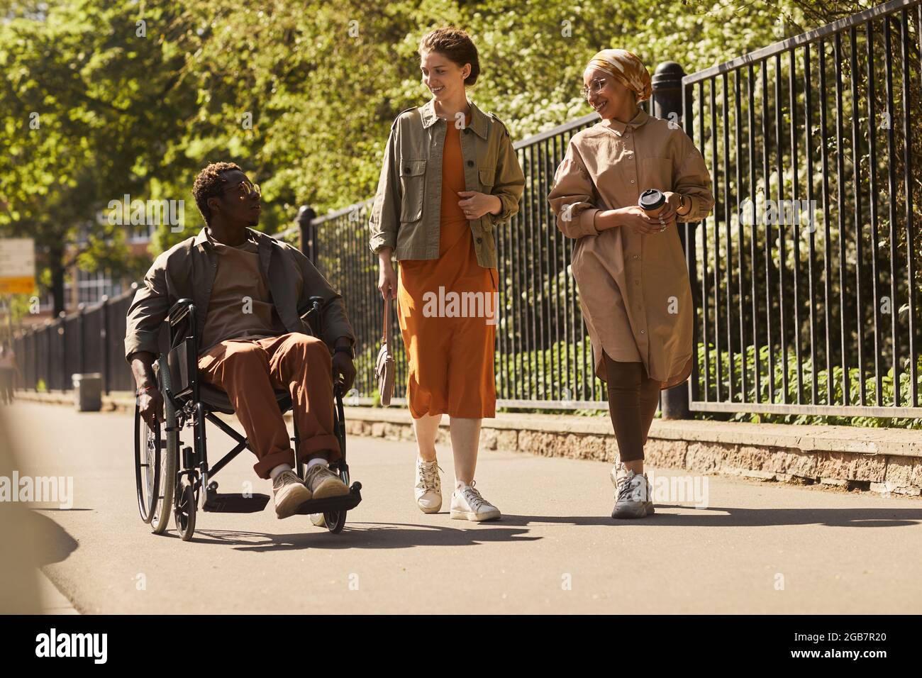 Young multi-ethnic friends walking together along street and talking to ...