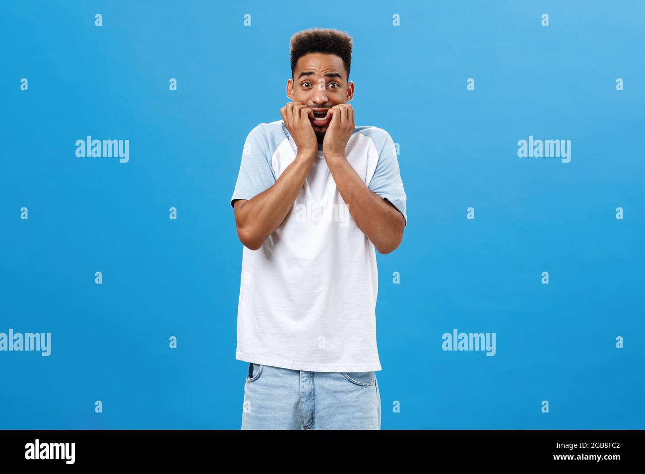 Portrait of frightened insecure dark-skinned guy having fobia biting ...