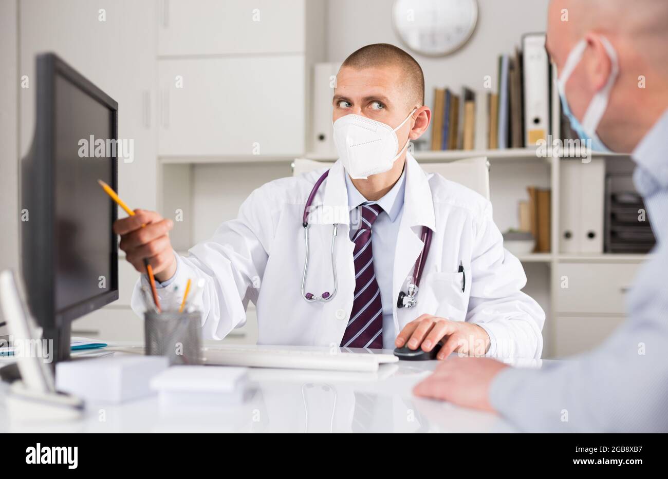 Male doctor in a protective mask consults a patient in the office Stock ...