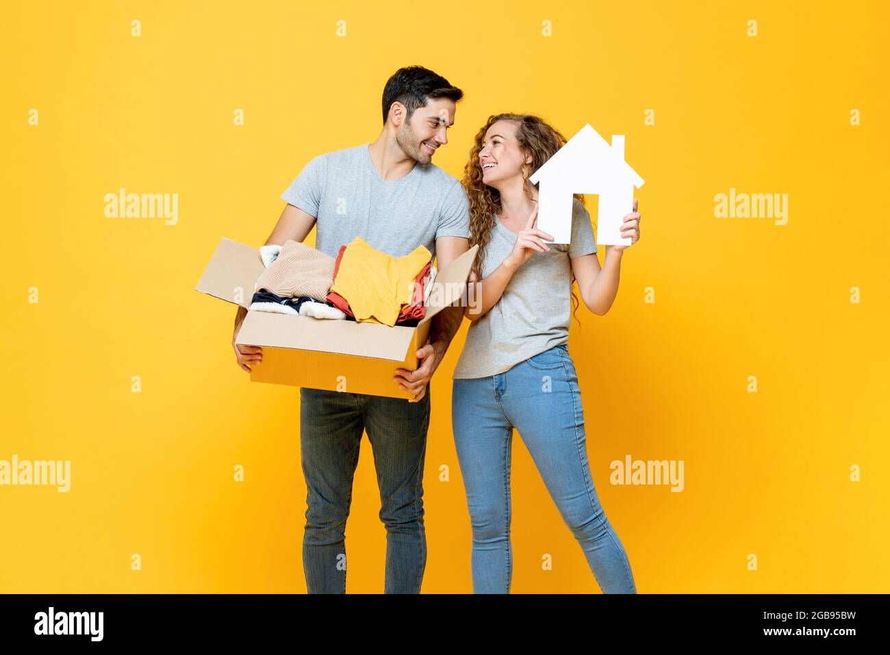 Happy cheerful young couple carrying stuff standing in yellow isolated ...