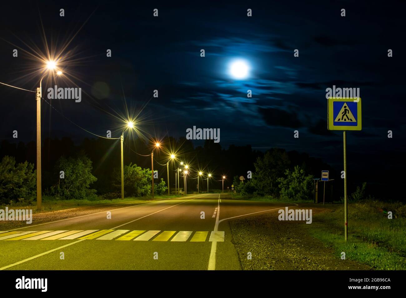 view of a night paved road with a pedestrian crossing on a moonlit ...