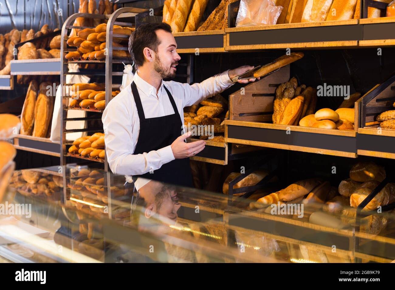 Male shop assistant demonstrating delicious loaves of bread in bakery ...