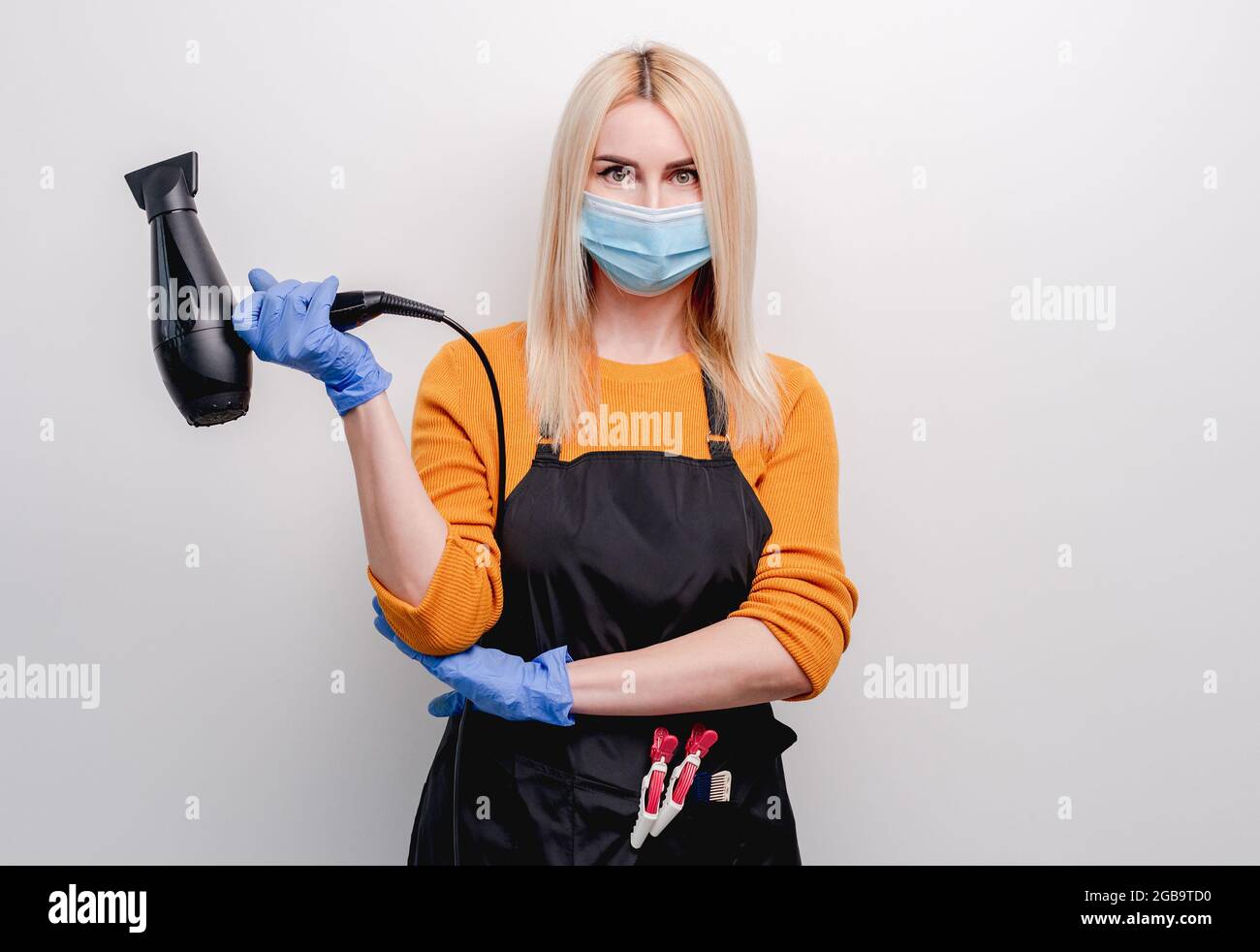 Blond woman hairdresser wearing medicine mask holding hair dryer in her ...