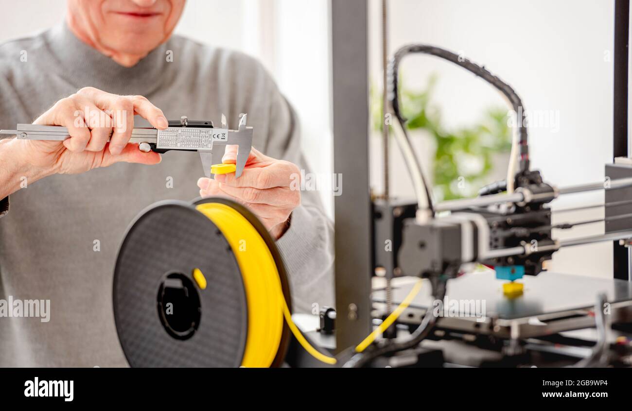 Man measuring size of yellow detail printing with modern 3D printer ...
