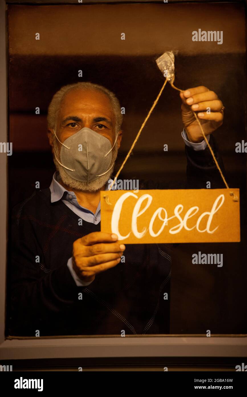 AN OLD MAN WEARING FACE MASK HANGING CLOSED SIGN BOARD Stock Photo - Alamy