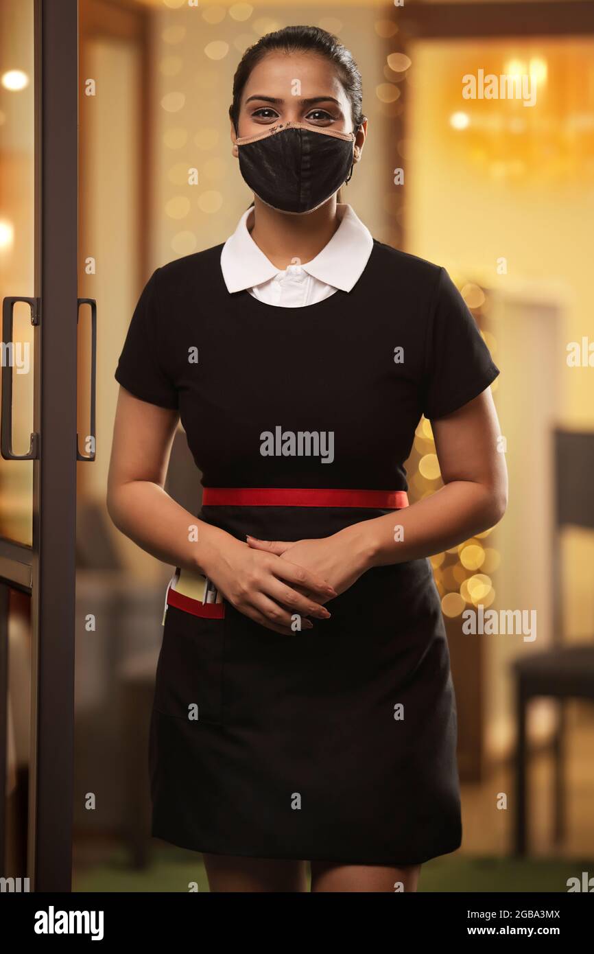 A YOUNG WAITRESS STANDING IN FRONT OF RESTAURANT WEARING FACE MASK ...
