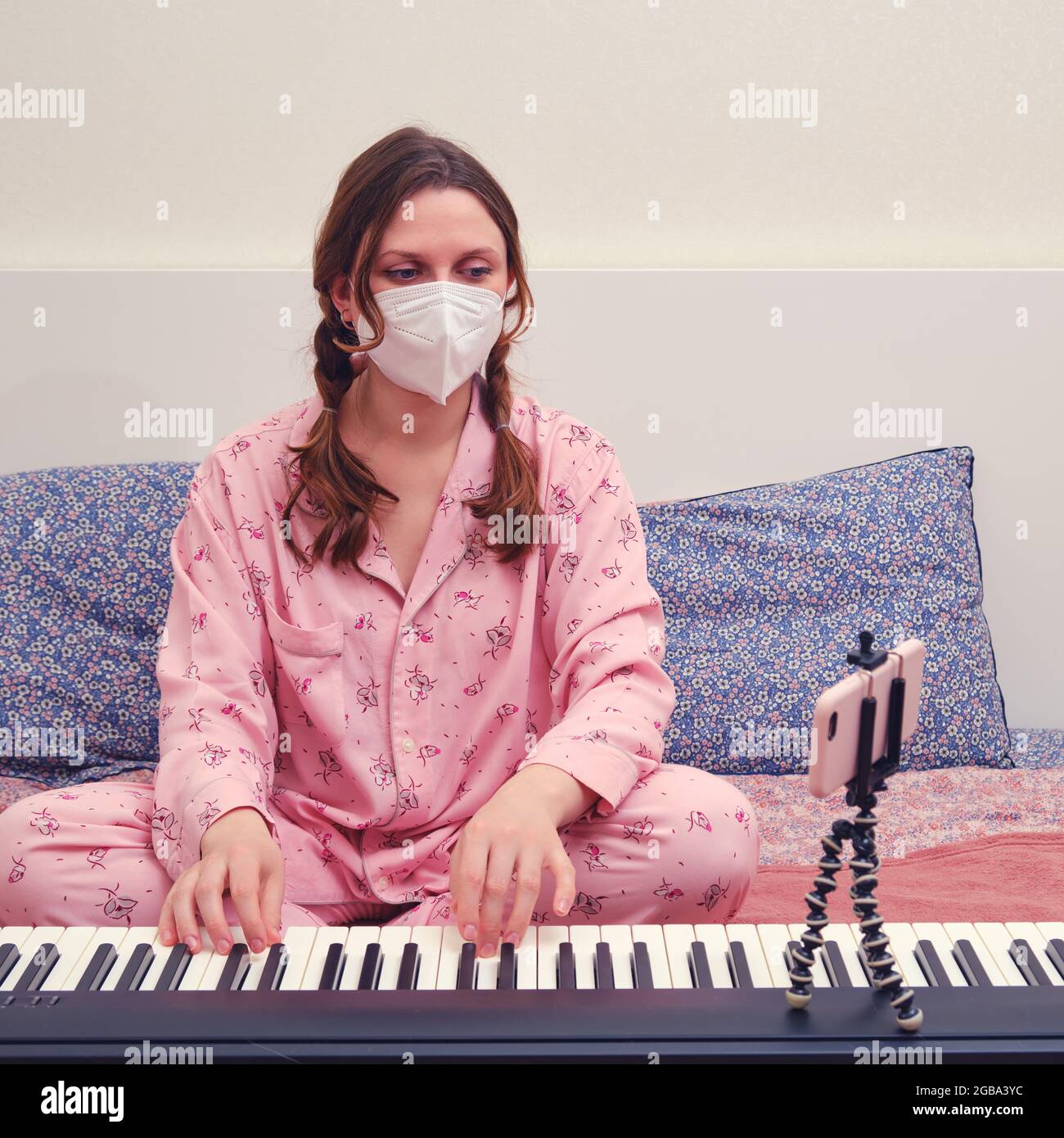 A woman wearing a face mask records piano lessons on her phone video ...