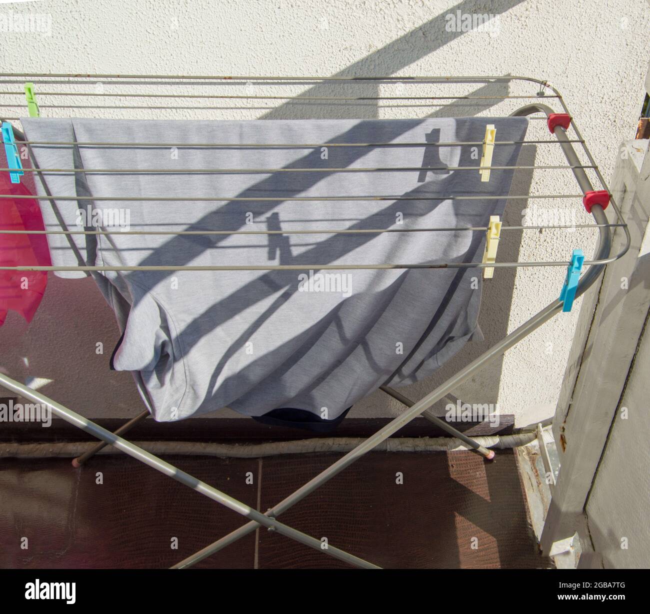 Washed men's T-shirt hanging on a metal dryer on the balcony, sunlight ...