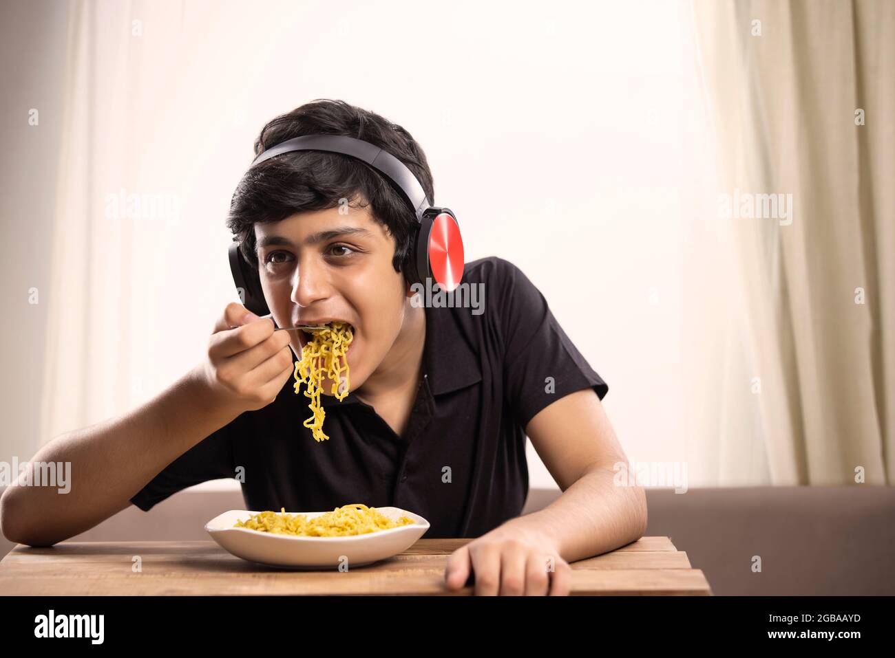 A TEENAGE BOY HAPPILY EATING MAGGI WHILE LISTENING TO MUSIC Stock Photo ...