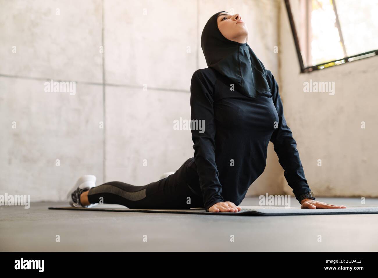 Young muslim woman in hijab doing exercise during yoga practice indoors ...
