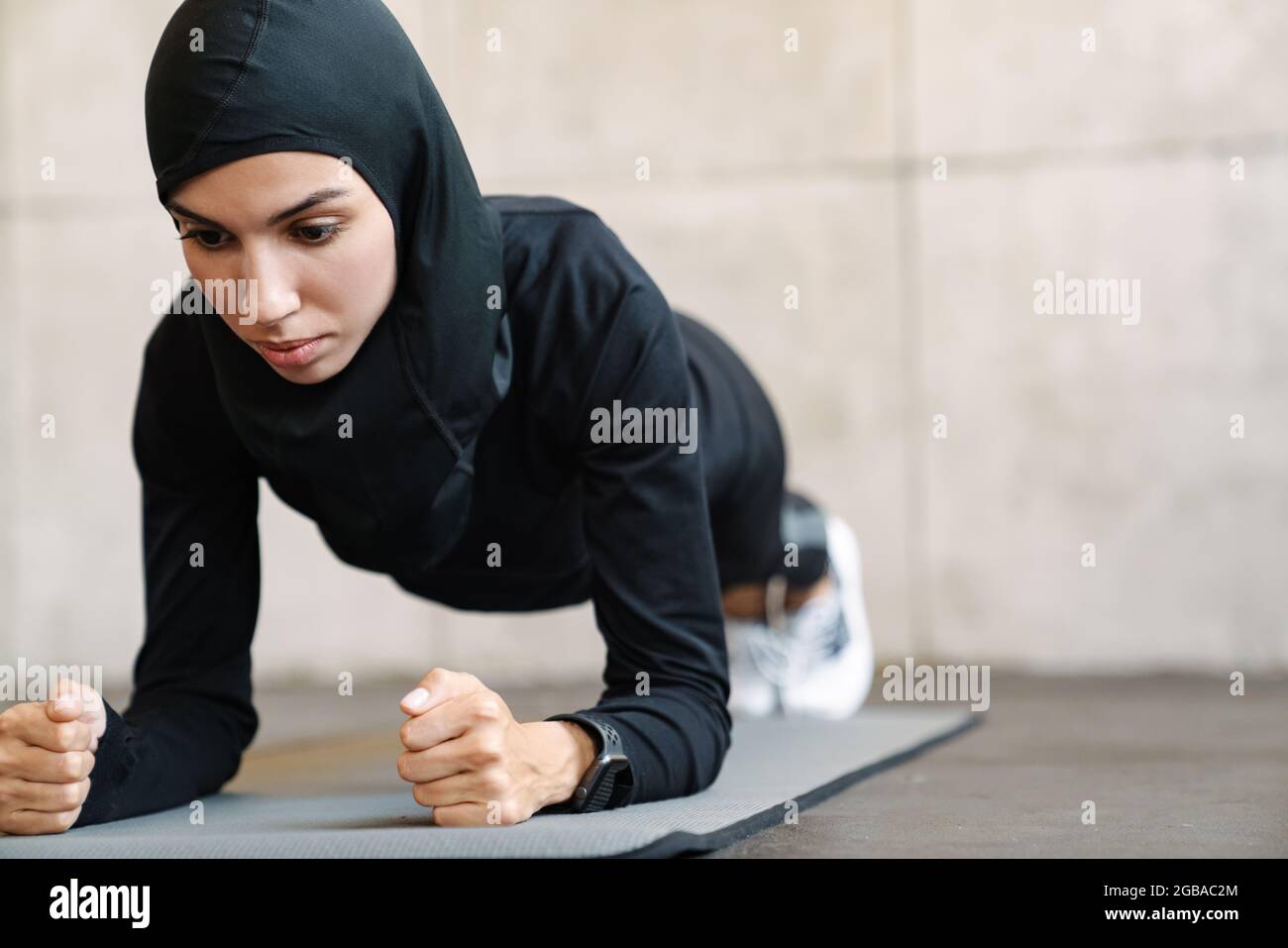 Young muslim woman in hijab doing exercise while working out indoors ...