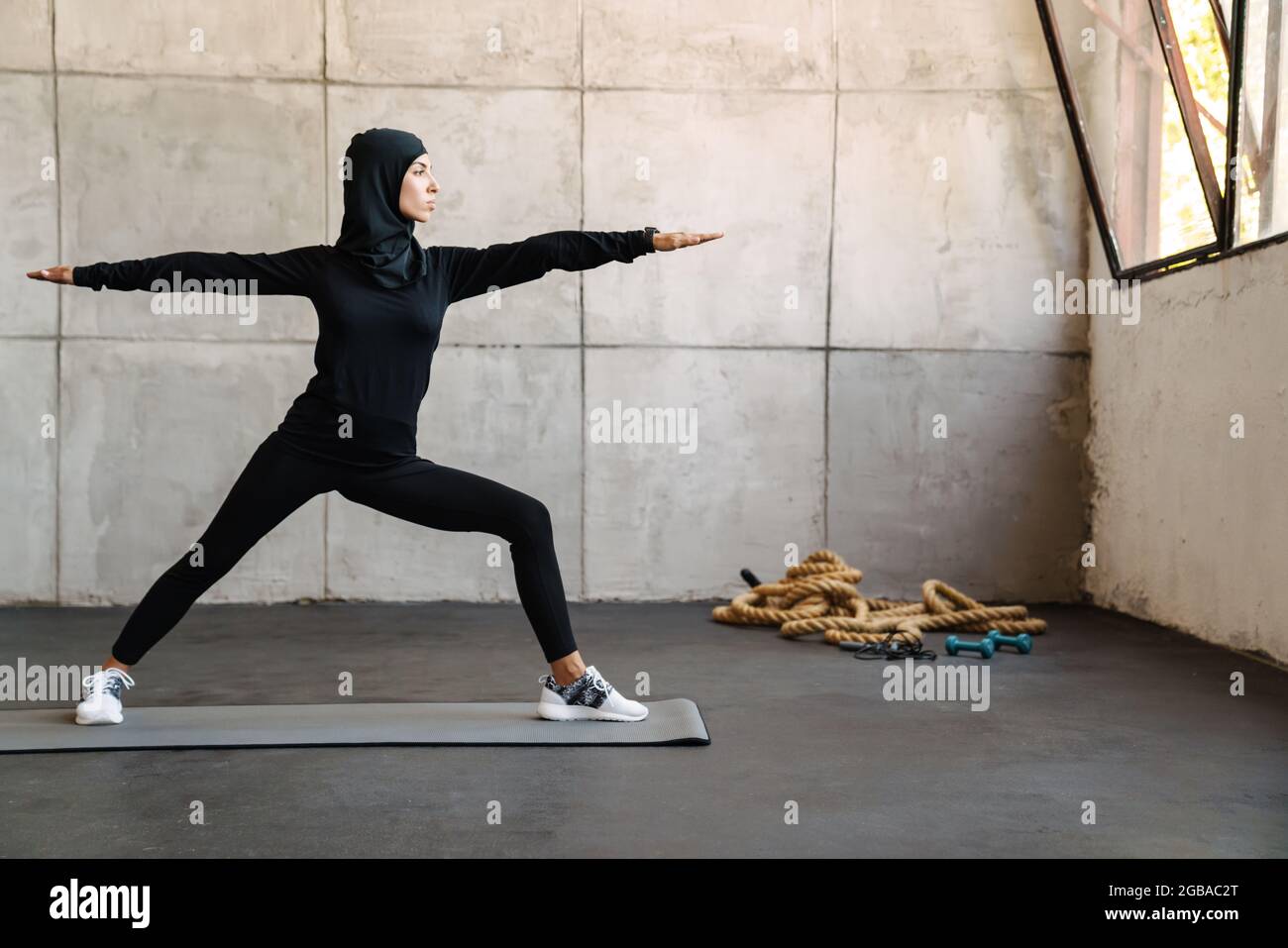 Young muslim woman in hijab doing exercise during yoga practice indoors ...