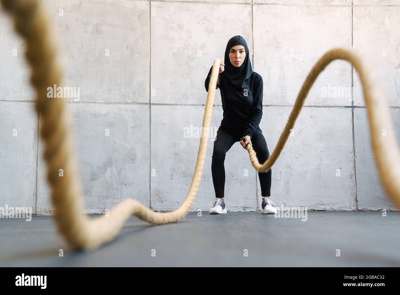 Young muslim woman in hijab working out with battle ropes indoors Stock ...
