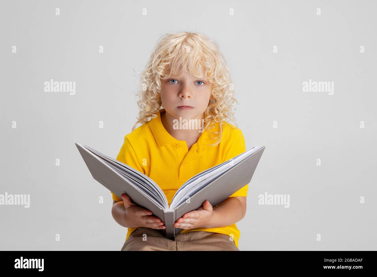Portrait of one cute little curly preschool boy reading book isolated ...