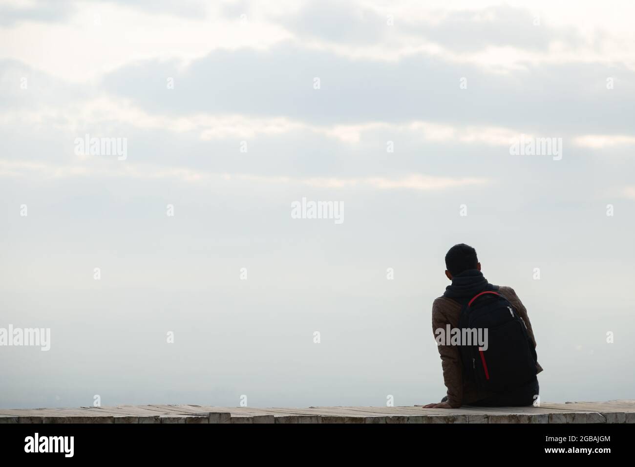 Young man sitting on edge mountain Stock Photo - Alamy