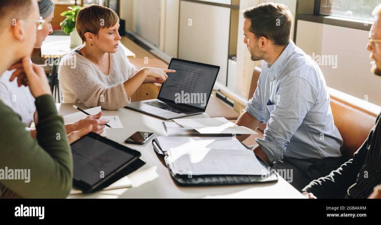 Manager pointing at laptop screen and talking to colleagues during ...