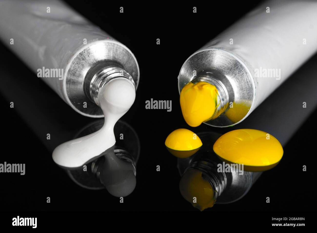 White and yellow paints follow from the tubes on black background close ...