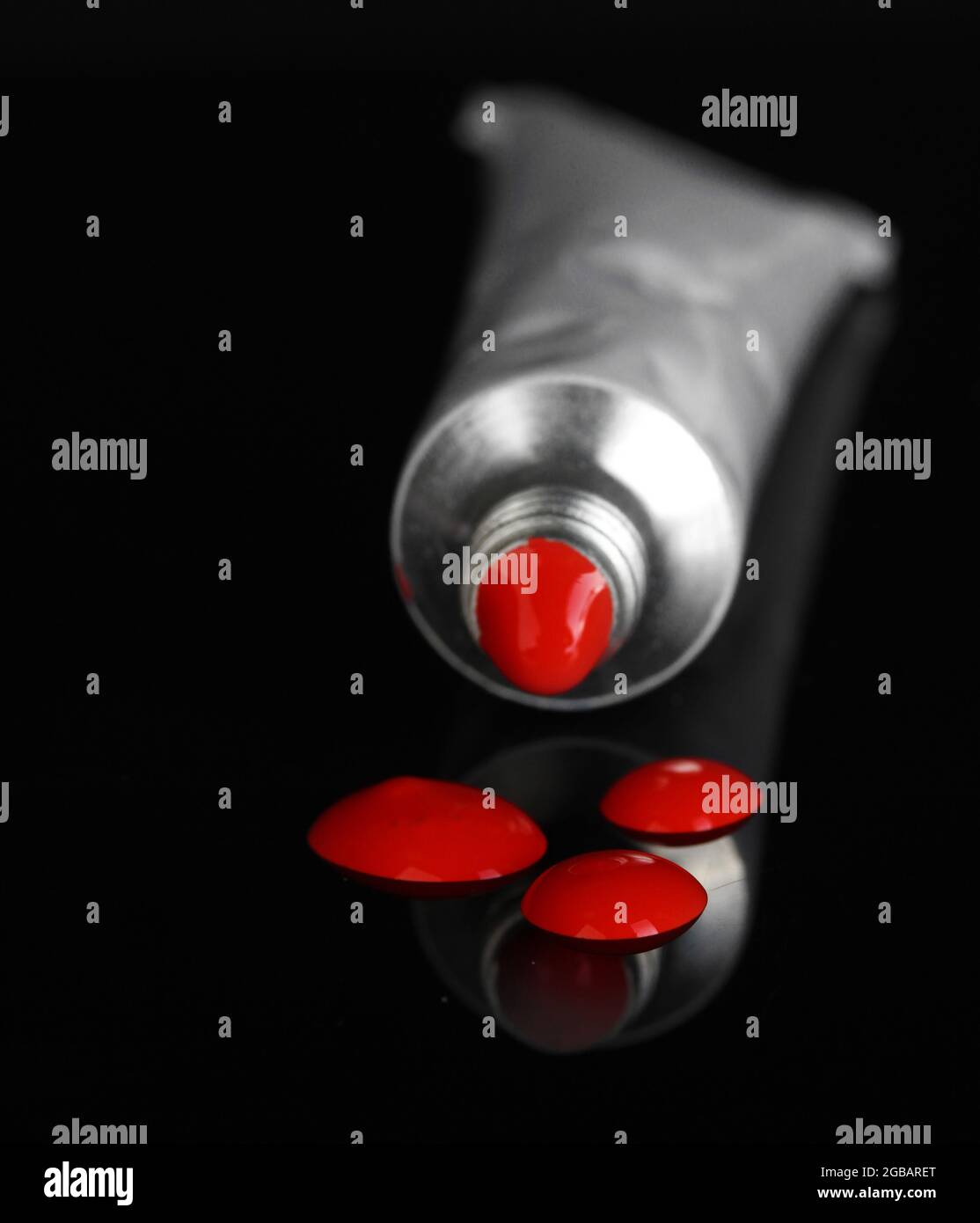 Red paint follows from the tube on black background close-up Stock ...
