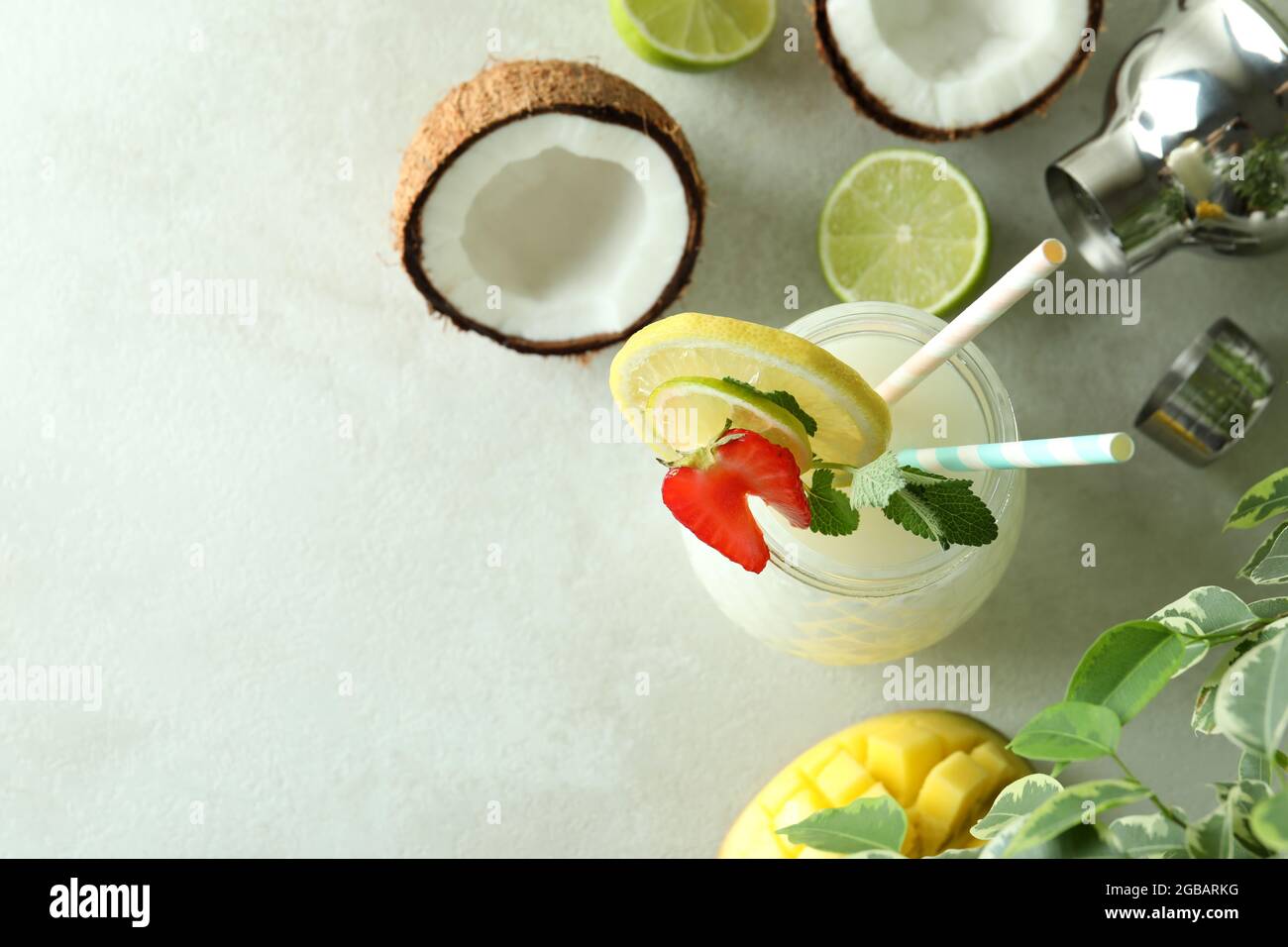 Glass of tropical cocktail and ingredients on white textured table ...