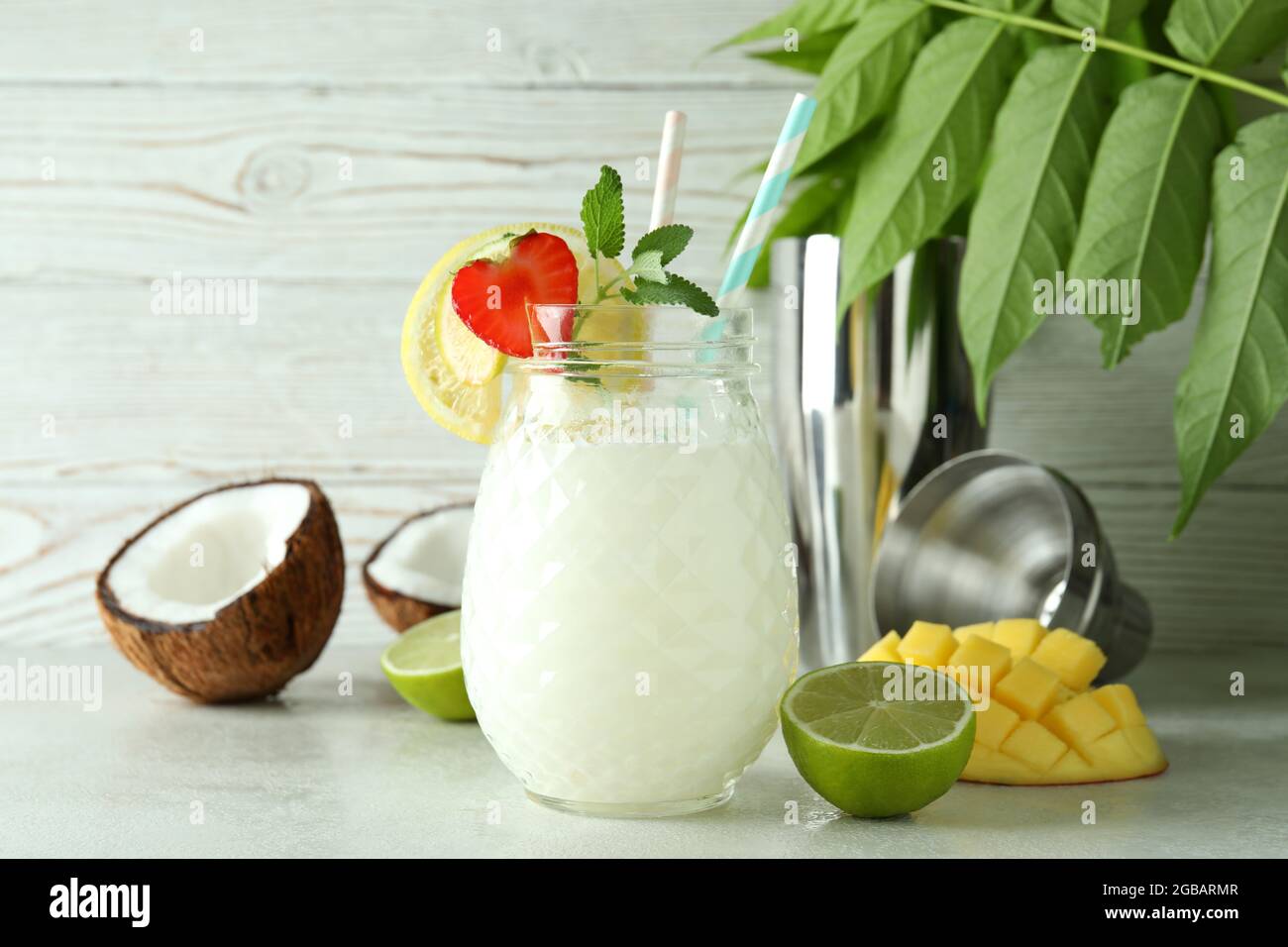 Glass of tropical cocktail and ingredients on white textured table ...