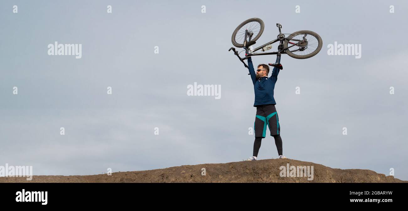 panorama Bearded cyclist on the mountain holds his bike in his arms ...