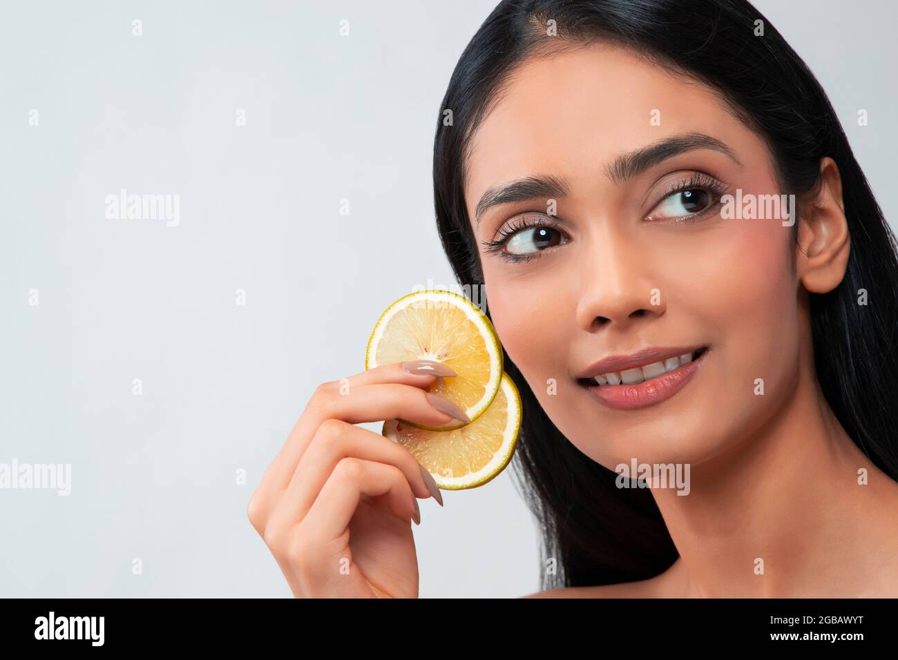 A young woman with clear,spotless skin holding two slices of lemon ...