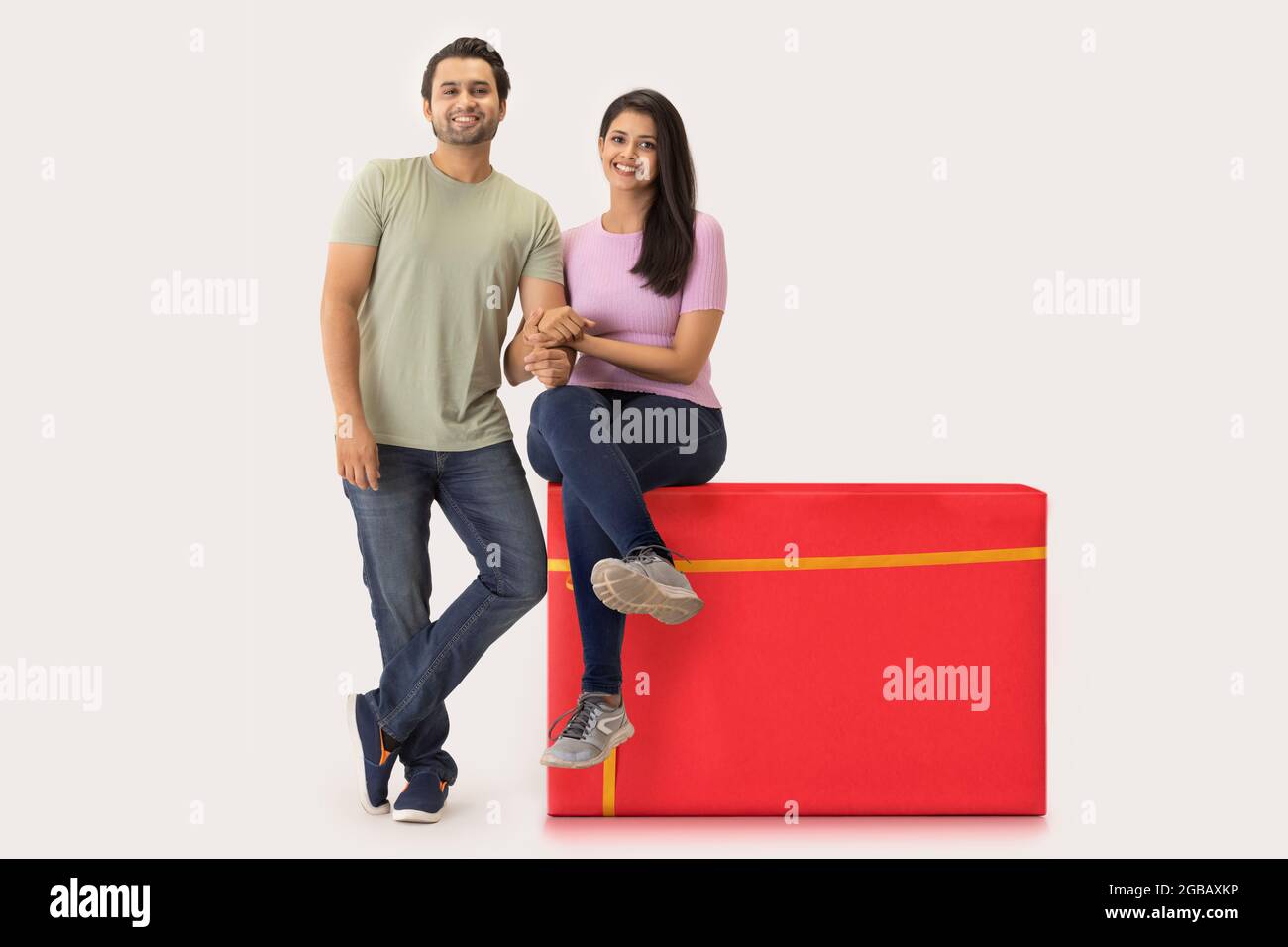 A young woman sitting on a gift shaped stool with a young man beside ...