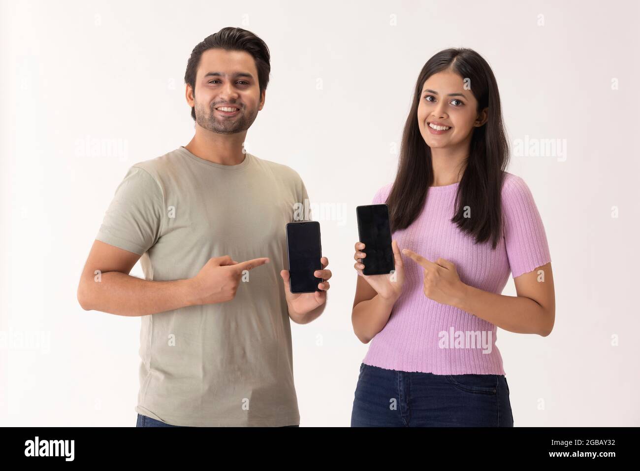 A young man and woman pointing to the mobile phones in their hands ...