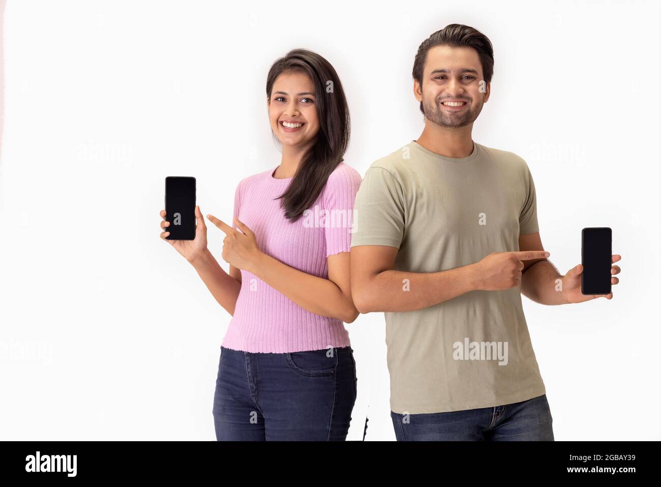 A young man and woman pointing to the mobile phones in their hands ...