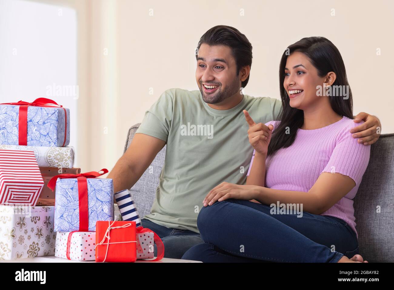 A young man and woman sitting happily in room with gift boxes beside ...