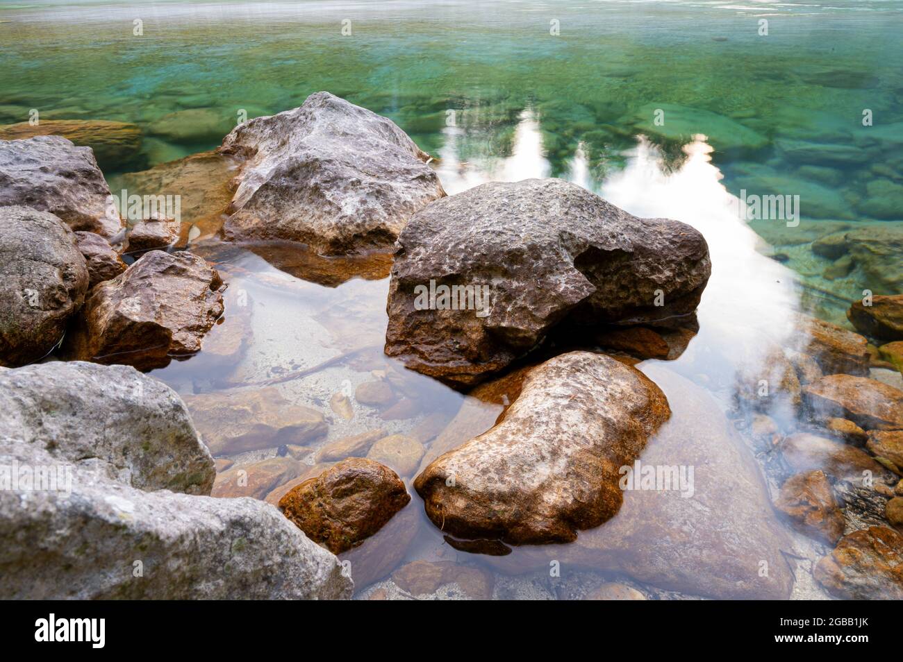 Rocks looking out a beautiful green river of Soca with trees reflecting ...