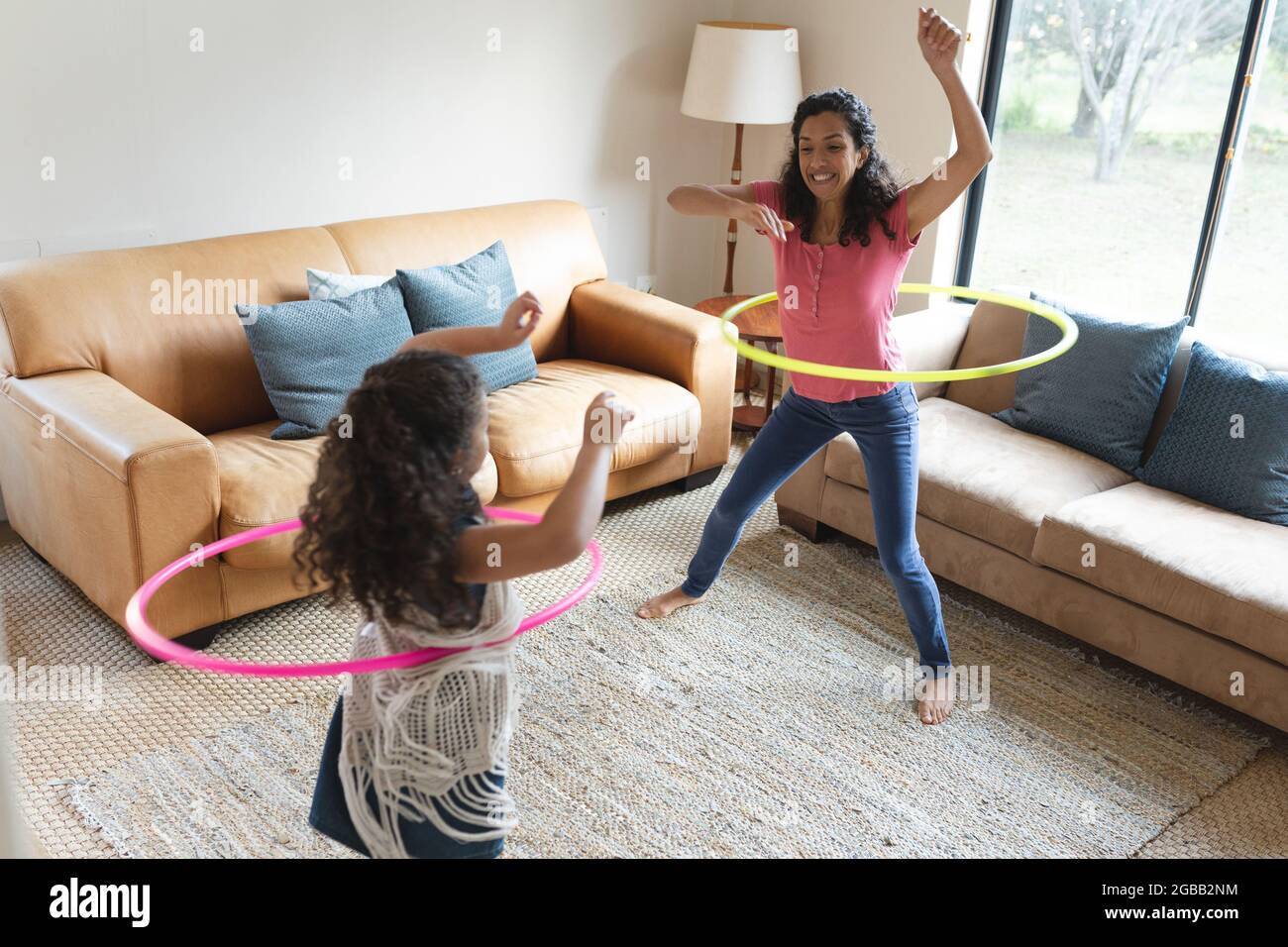 Happy mixed race mother and daughter playing with hula hoop in living ...