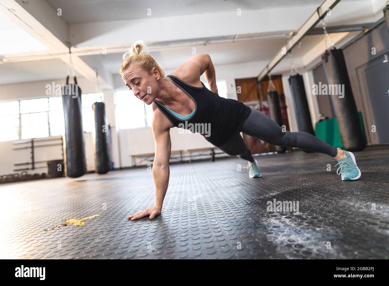 Strong caucasian woman exercising at gym, doing push-ups using one hand ...