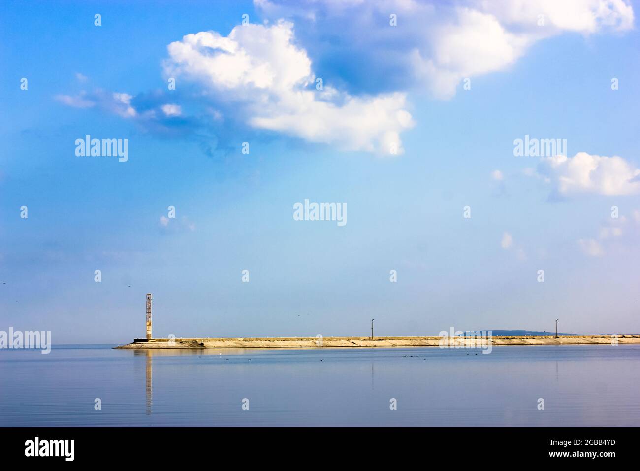 A concrete breakwater in a blue sea on a sunny day against a cloudy sky ...
