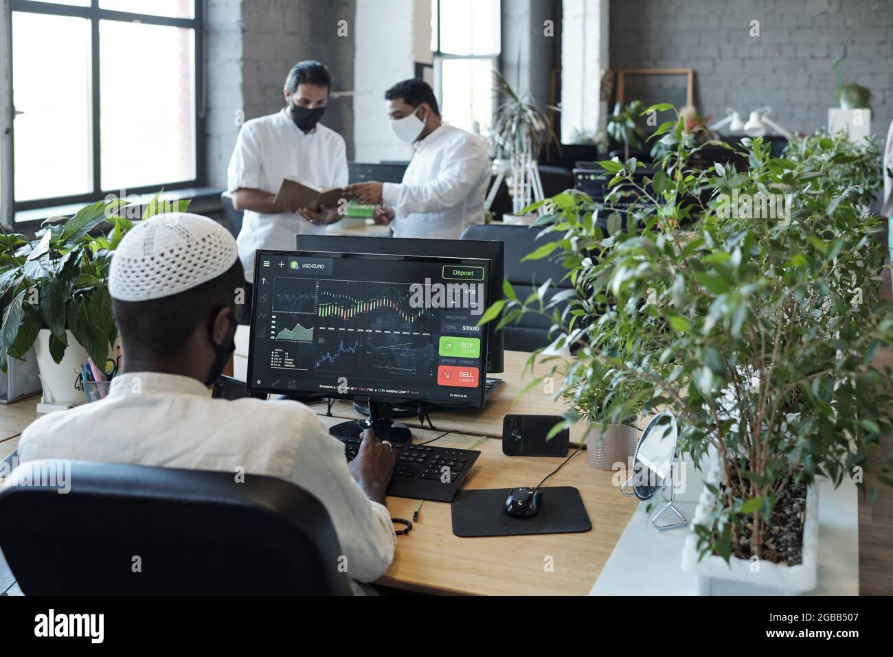 Rear view of young Muslim businessman sitting in front of computer ...