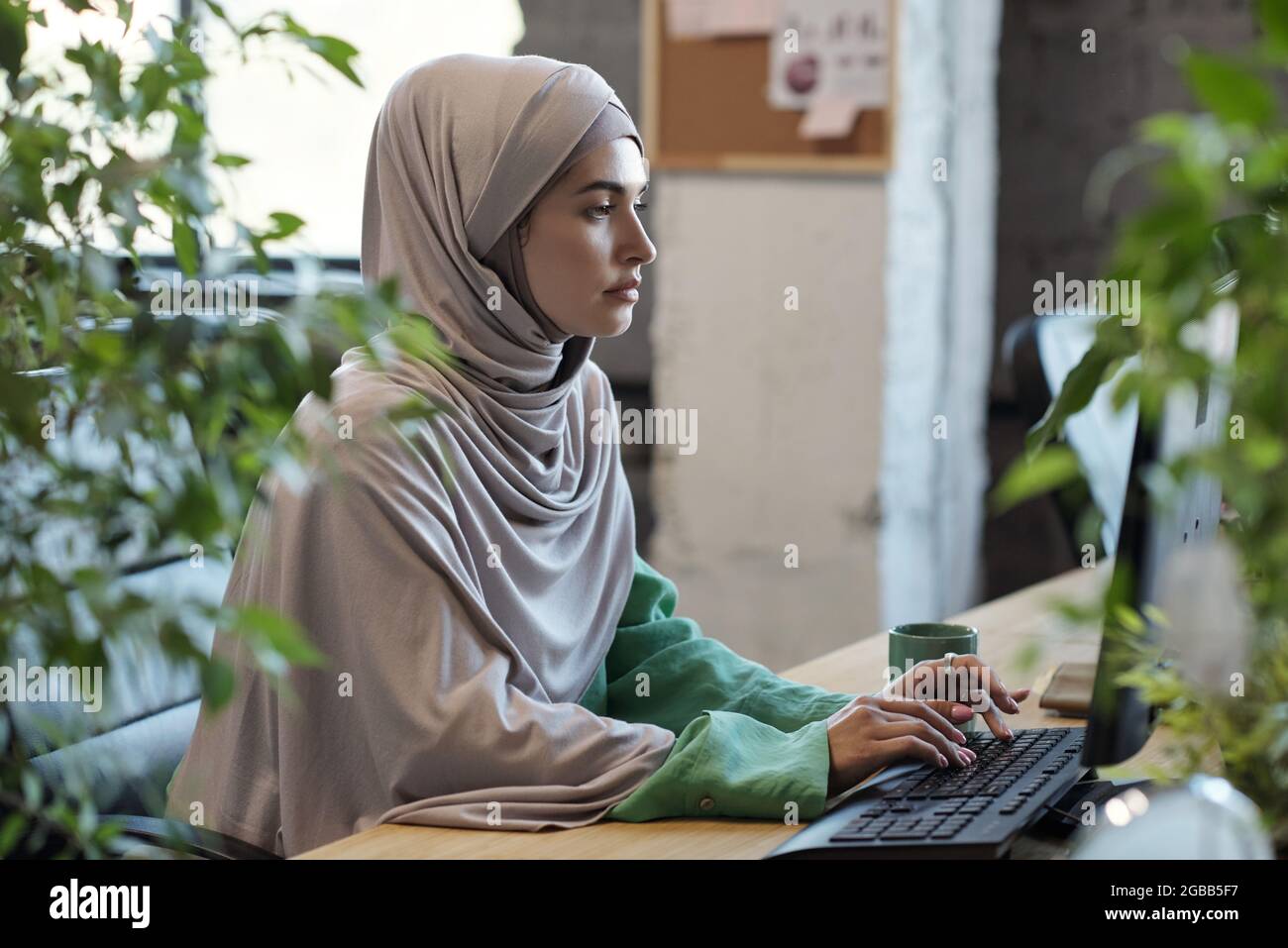 Serious Muslim female in hijab looking at computer screen while ...