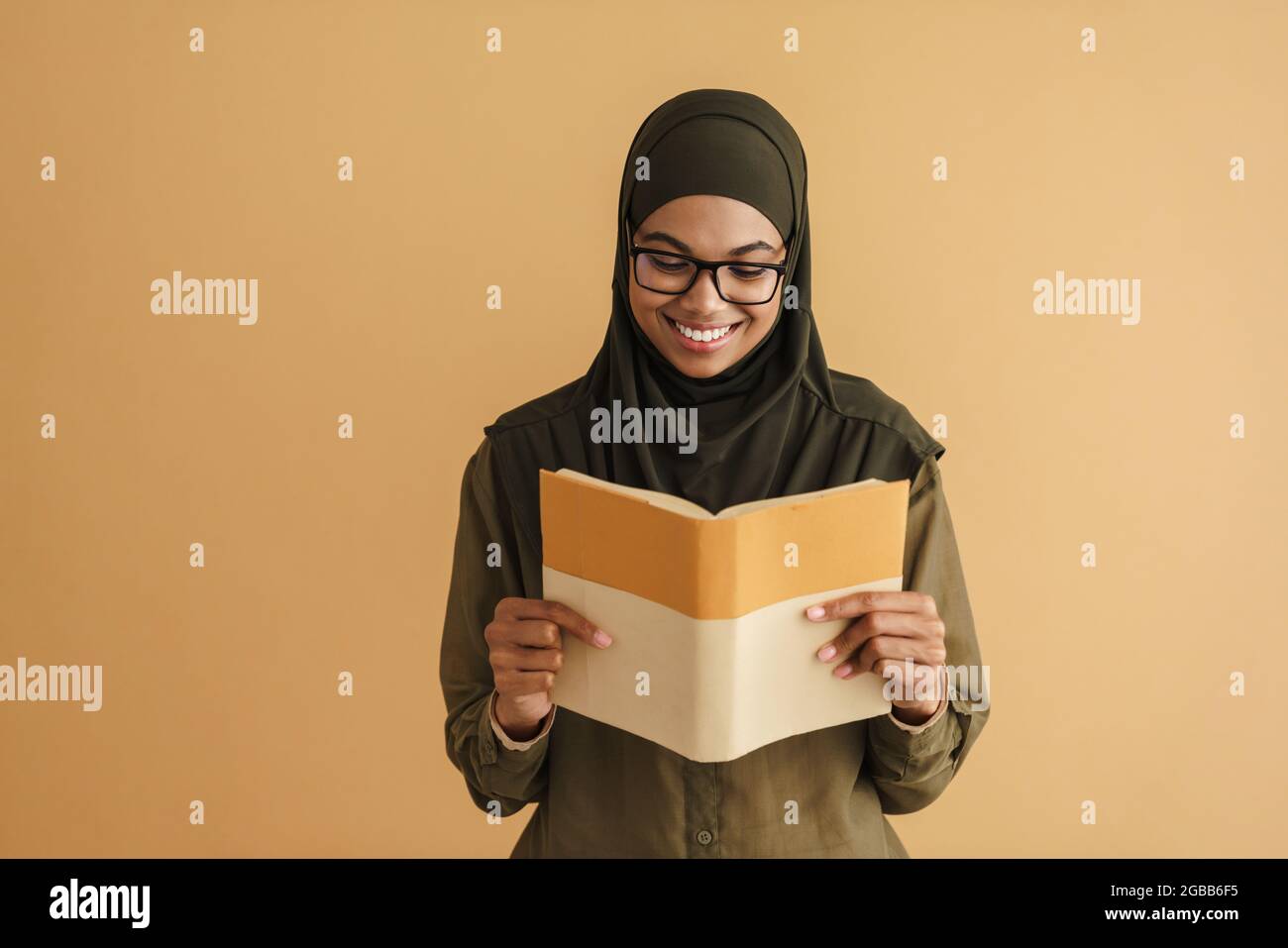 Black muslim woman in hijab smiling while reading book isolated over ...