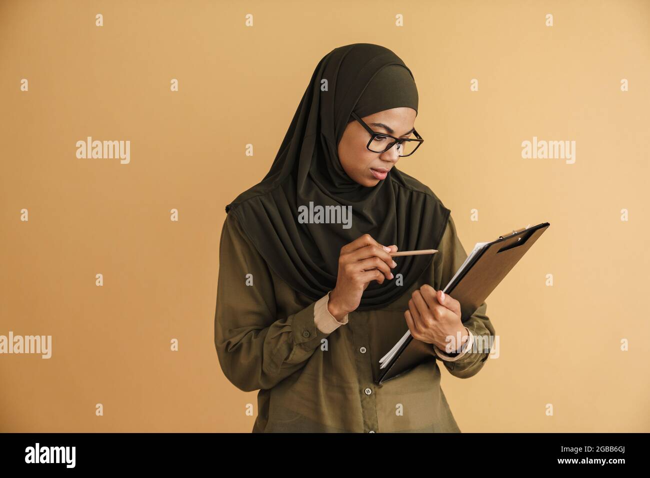 Black muslim woman in hijab posing with clipboard isolated over beige ...