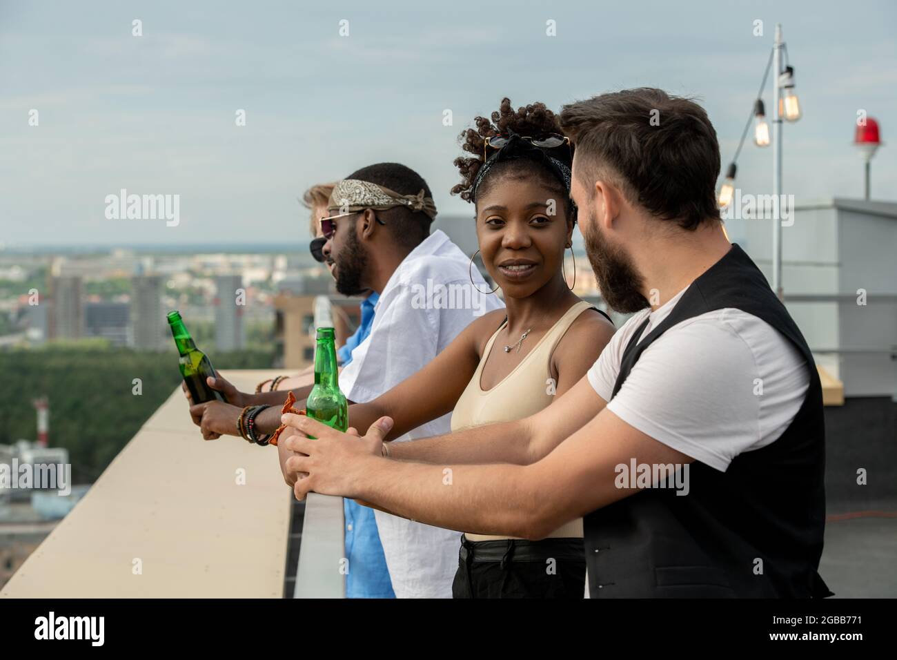 Young intercultural friends having beer on balcony at outdoor party ...